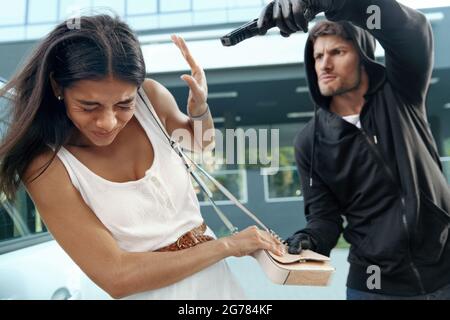 Aggressive robber want to steal handbag of frightened girl. Male bandit ...