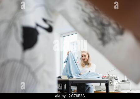 smiling designer looking at tissue sample near colleague measuring ...