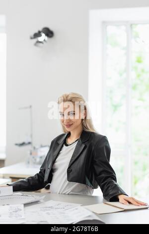 Designer looking at notebook near sewing patterns on blurred foreground ...