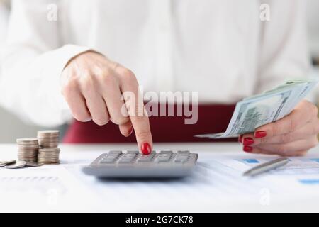 Woman calculates on calculator and holds cash in hand at work table ...