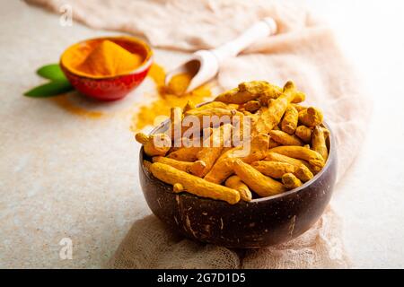 Dried turmeric roots in coconut shell bowl and powder with leaves on a ...
