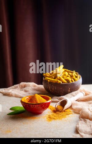 Dried turmeric roots in coconut shell bowl and powder with leaves on a ...