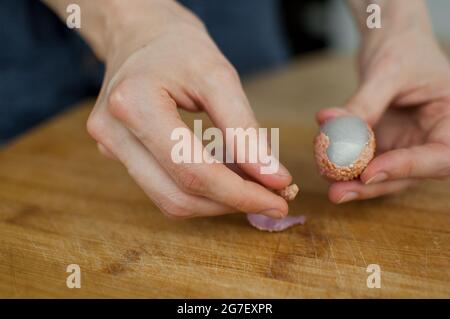 Female hands hold a litchi fruit, lychee on a wooden desk. Exotic ...