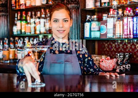 Cheerful female barkeeper with glass of refreshing vermouth standing at ...