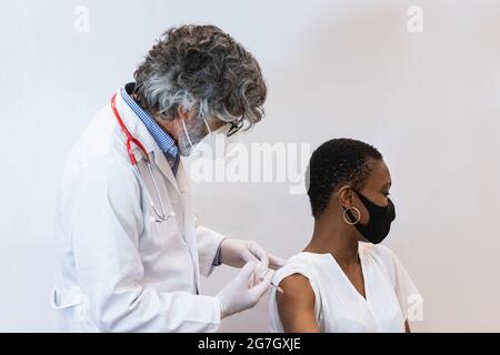 Male medic making injection for black female patient in mask Stock ...