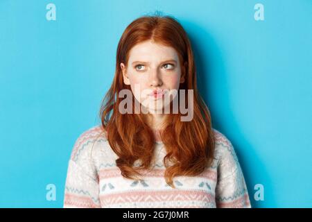 Serious redhead girl thinking, grimacing and frowning while pondering ...