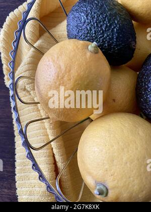 Vertical shot of avocadoes and lemons in a metal bowl on a yellow towel ...