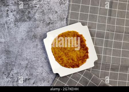 Potato pancake on a white square plate on a dark background. Top view ...