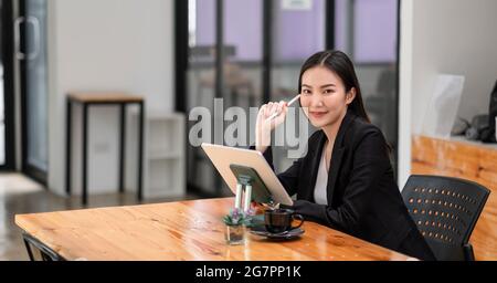 Happy freelance worker woman holding smartphone, sitting at work table ...