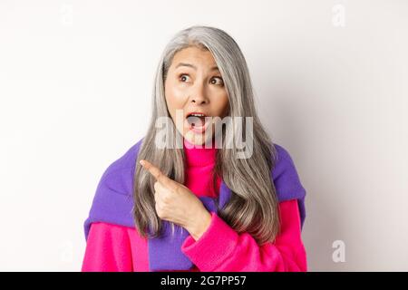 Close-up of amazed and intrigued asian senior woman pointing finger ...
