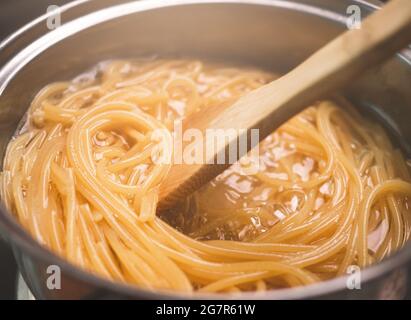 Raw spaghetti is being cooked in boiling water in a kitchen pot ...