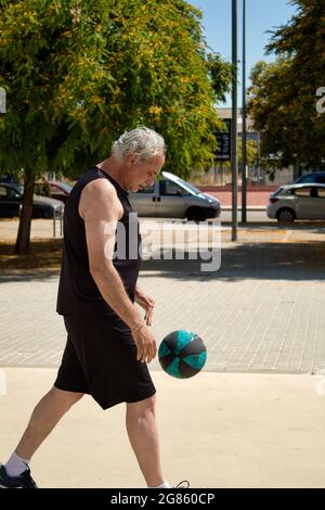 mature man training basketball alone on a street court with metal ...