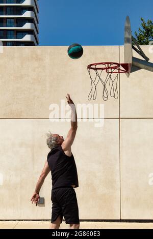 mature man playing basketball alone on a street court with metal basket ...