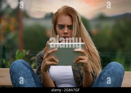 Horrified young woman staring wide-eyed at her tablet Stock Photo - Alamy