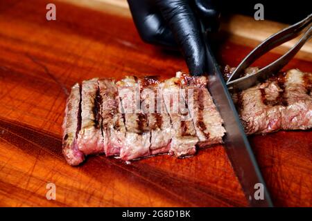 Picanha or Rump Steak. Hand with black gloves cutting a juicy steak on ...