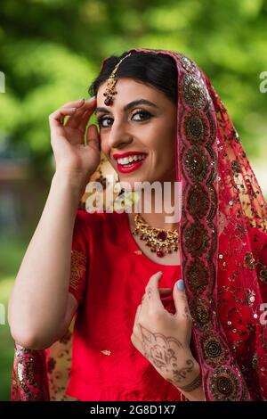joyful indian bride in red sari holding traditional headscarf with ...