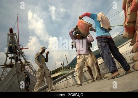 Workers are transporting cement sacks from a truck onto a phinisi ship ...