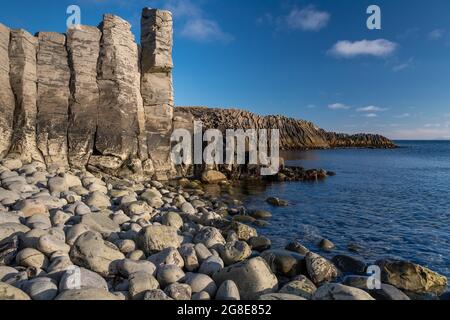 Basalt cliff, beach with rounded stones and lighthouse, Kalfshamarsvik ...