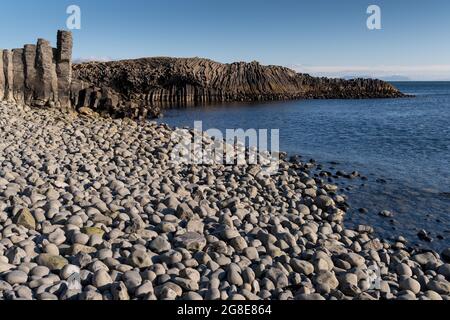 Basalt cliff, beach with rounded stones and lighthouse, Kalfshamarsvik ...