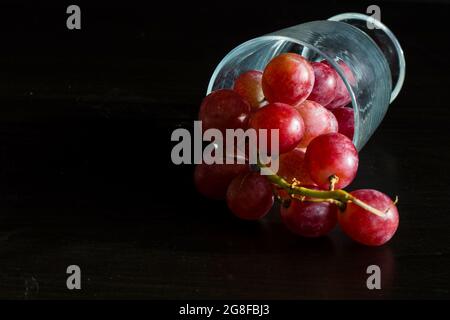 Red grapes in a glass fallen on a black background Stock Photo - Alamy