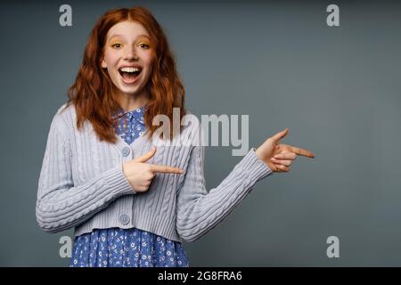 Young ginger excited woman exclaiming and pointing finger upward ...