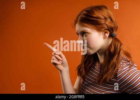 Young ginger displeased woman pointing finger at her face isolated over ...