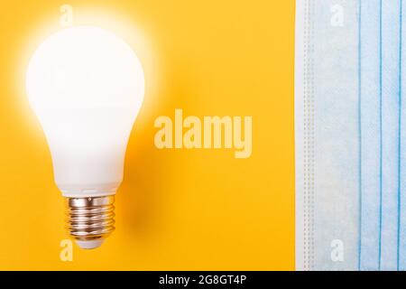 Glowing Power Saving Lamp with Medical Face Mask Lying on Yellow ...