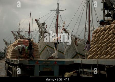 Workers transporting cement sacks from a truck onto a phinisi ship at ...