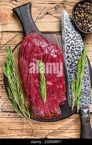 Elk raw steak from wild meat on a cutting board. Wooden background. Top ...