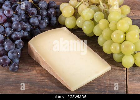 French comté cheese with black grapes on wooden background Stock Photo ...