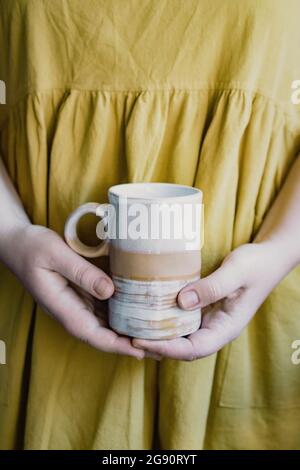 A person holds a white ceramic cup in one hand and a sucrose cube in ...