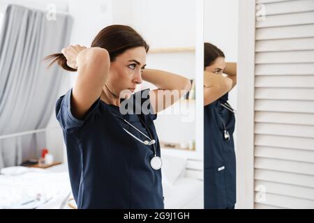 Focused mid woman doctor in medical suit doing hair at home Stock Photo ...