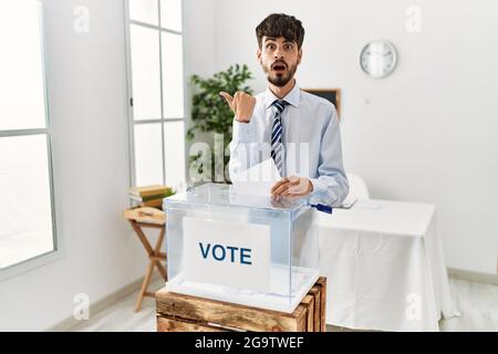 Hispanic man with beard voting putting envelop in ballot box pointing ...