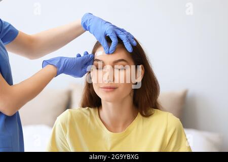 Nurse applying medical patch on young woman's forehead in clinic Stock ...