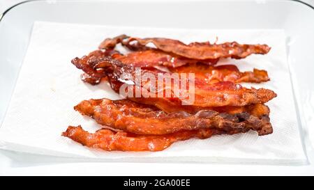 Step by step. Cooked bacon strips on a white tray with a paper towel ...