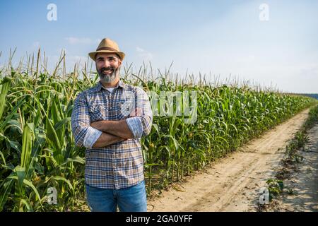 Proud farmer is standing in his growing corn field. He is satisfied ...