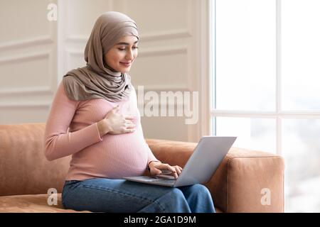 Pregnant Muslim woman sitting on sofa at home Stock Photo - Alamy