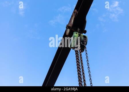 Green chain fall hoist on an I-beam silhouetted against a pale blue sky ...