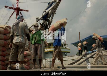 Workers are transporting cement sacks from a truck onto a phinisi ship ...