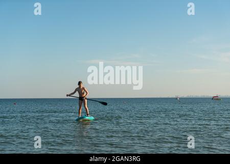 A 12 year old boy learns to stand on a SUP board in the sea near the ...