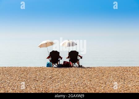 isolated couple sitting under sun shade umbrellas on pebble beach at St ...