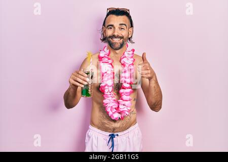 Young hispanic man wearing swimsuit and hawaiian lei drinking tropical ...