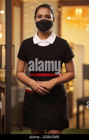 Young black waitress in face mask standing by cafe counter indoors ...