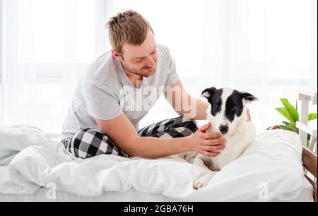Handsome man lying with dog at bed. Young man in a bed under a rug with ...