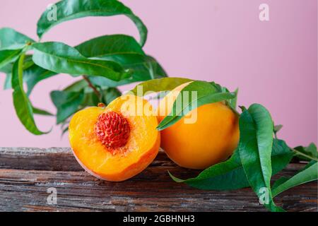 Peach in halves with bone. Peaches with leaves on wooden board. Ripe ...