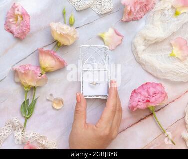 Woman hand opens a gift box with a pearl ring with light pink flowers ...