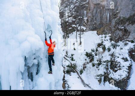 Male athlete doing a vertical ice climb, kicking front crampons into ...
