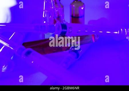 Syringes on a purple surface with reflections in it in a dark room ...