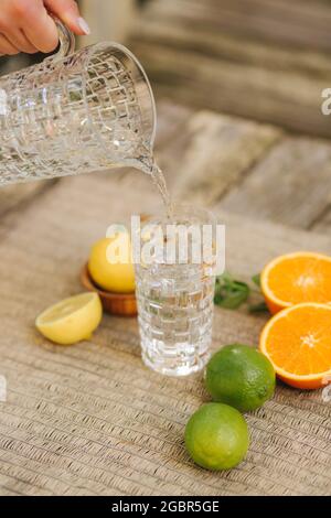 Proces of pouring cold water into a tall glass. Fresh citrus on table ...