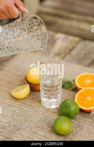 Proces of pouring cold water into a tall glass. Fresh citrus on table ...